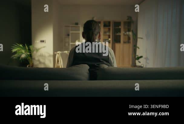 Person seen from behind sitting on a sofa in a calm living room with ...