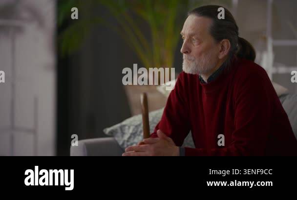 Senior man in profile resting at home, holding a cane and looking away ...