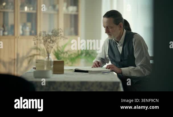 An older man sits at a dining table and reviews papers in a calm home ...