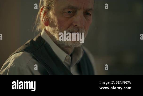Close up of an older bearded man indoors, looking down with a serious ...