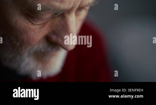 Close-up of an elderly bearded man looking downward in soft indoor ...