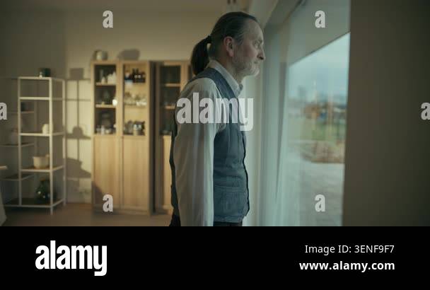 Profile view of an older man standing near a large window in a softly ...