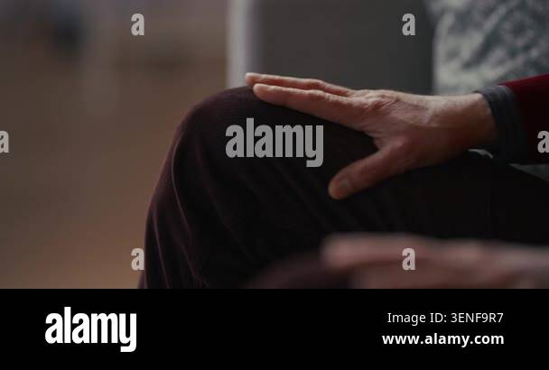 A close-up shows a hand resting on a bent knee in a calm indoor setting ...