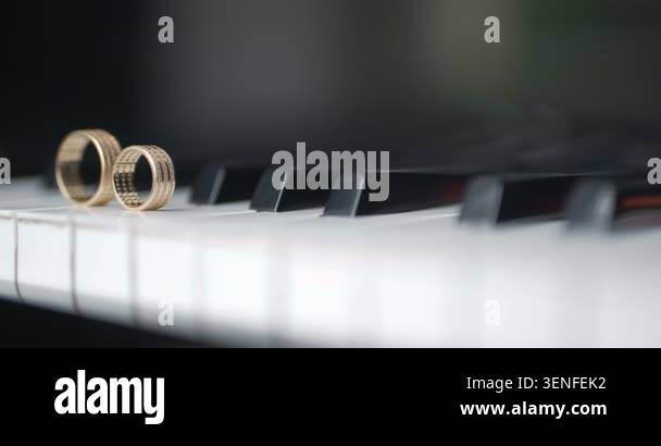 Two gold wedding rings resting on piano keys with warm side lighting ...