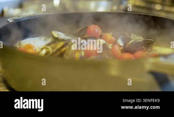 Close-up of mussels and cherry tomatoes simmering in a pan with rising ...