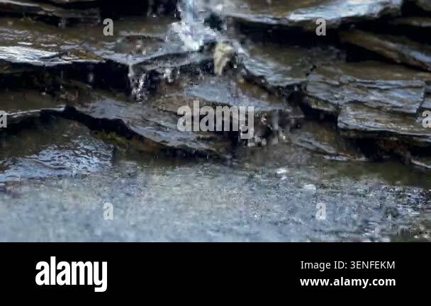 Close-up of clear water flowing over layered dark stones in a rocky ...