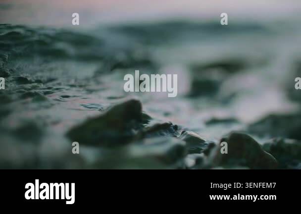 Close-up of dark wet rocks in the foreground with softly blurred water ...