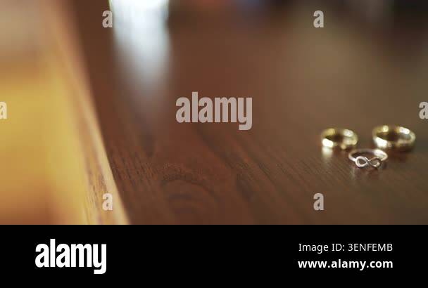 Two metallic rings rest on a warm wooden surface in shallow focus, with ...
