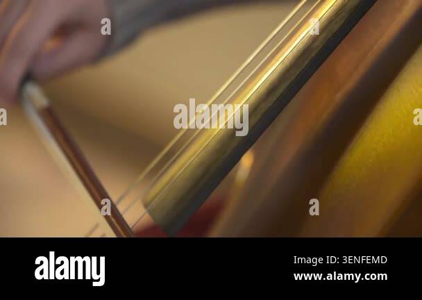 Close-up of a hand drawing a bow across the strings of a bowed string ...