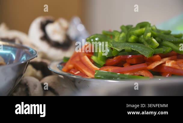 Close-up of sliced green and red peppers piled in a metal bowl, with ...