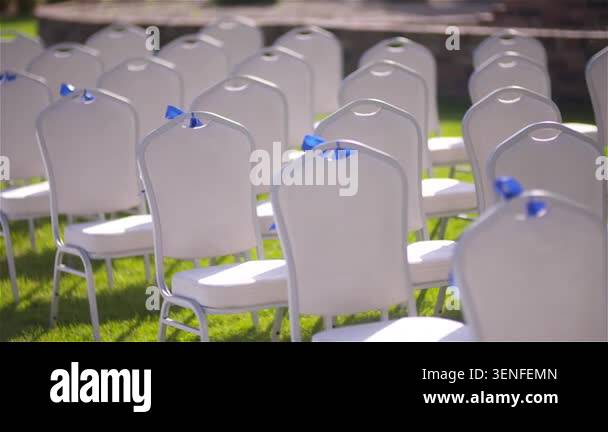 Rows of white chairs are neatly arranged on grass in bright sunlight ...