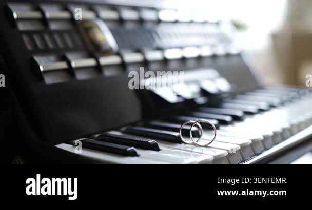 Two gold wedding rings rest on white piano keys in a softly lit close ...