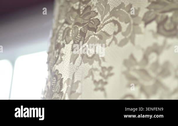 Close-up of a delicate floral lace textile hanging near a bright window ...