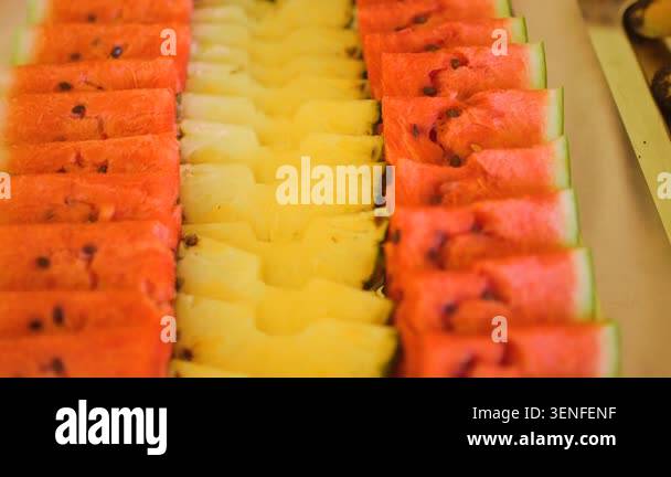 Neatly arranged rows of watermelon and pineapple slices on a tray ...