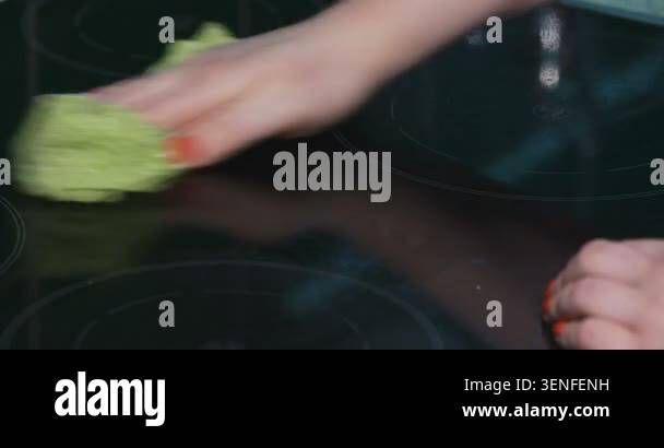 Close-up of hands cleaning a dark glass cooktop with a cloth in a ...