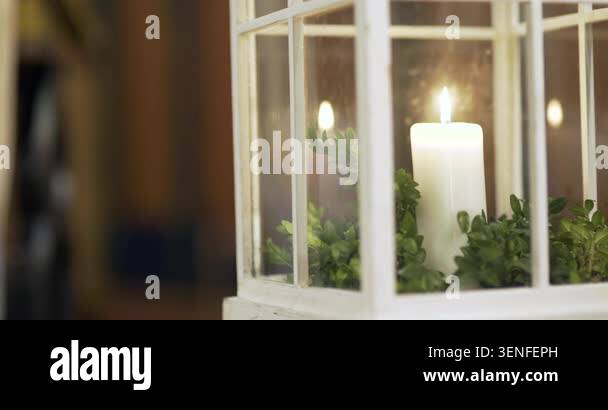 A single white candle burns inside a white glass lantern, surrounded by ...