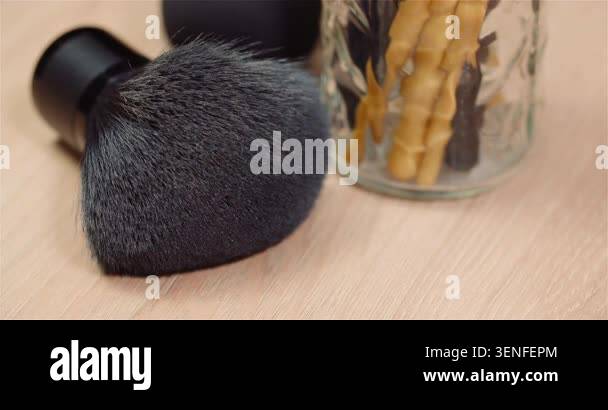 Close-up of a makeup brush resting on a wooden tabletop next to a glass ...