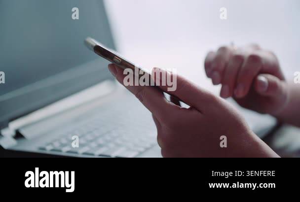 Close-up of hands holding and using a smartphone above a laptop ...