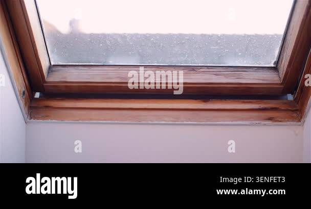 Upward view of a wooden skylight window inside a home, with raindrops ...