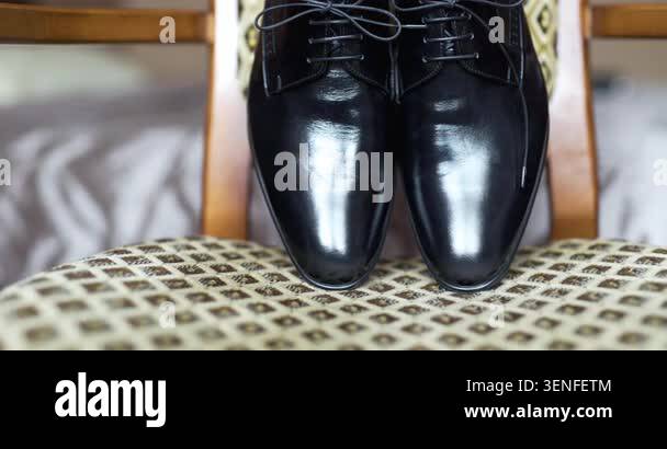 Shiny black lace-up dress shoes rest on a patterned upholstered chair ...