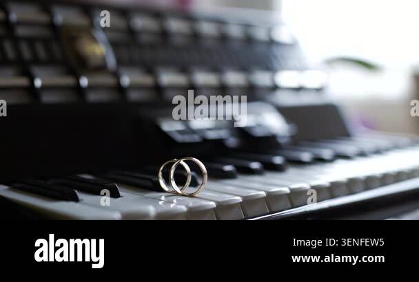 Two gold wedding rings rest on white piano keys in soft window light ...