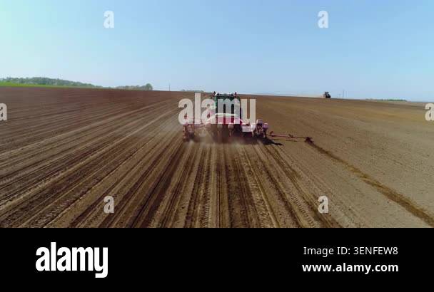 Rear view of a tractor working across a wide farmland field, cutting ...