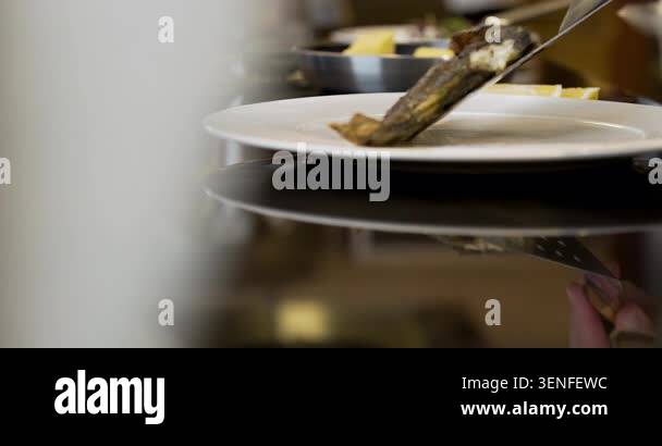 A plated fish meal is being presented on a white plate in a warmly lit ...