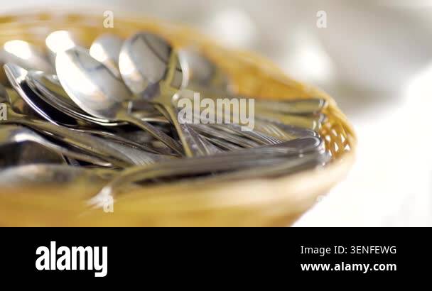 Close-up of shiny metal spoons and other cutlery resting in a woven ...