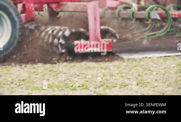 A rotary tiller breaks up muddy earth in a rural field, throwing soil ...