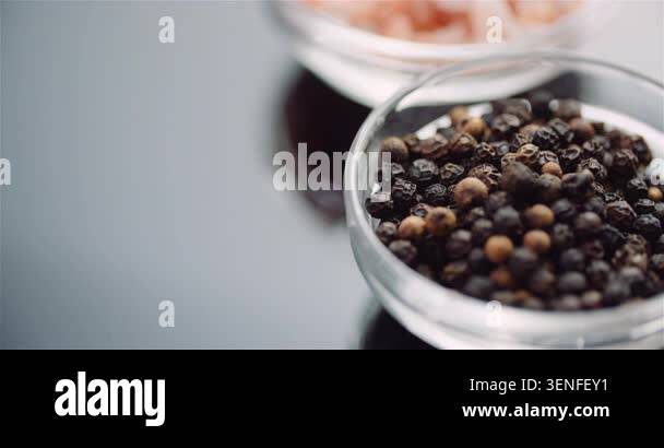 Clear glass bowl filled with peppercorns in the foreground on a gray ...