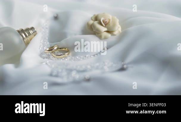 Softly lit arrangement of a perfume bottle, gold rings, pearl beads ...