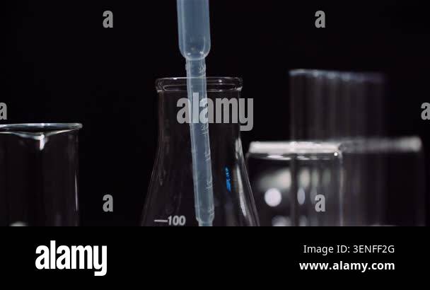 Close-up of clear laboratory glassware with a pipette centered above a ...