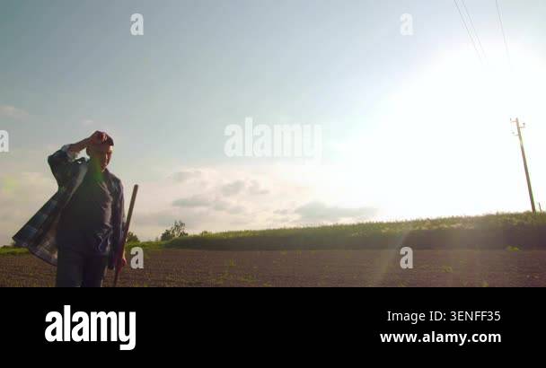 A lone man stands in an open countryside field, raising his hand to ...