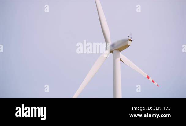 A single white wind turbine stands in an open outdoor setting with ...