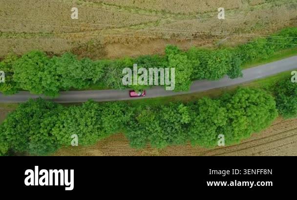 Top-down scene of a red car driving along a narrow rural road bordered ...