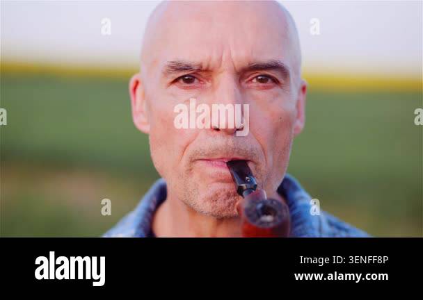 Close up portrait of a bald middle aged man holding a pipe in his mouth ...