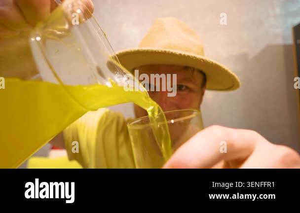 Pour yellow lemonade from a jug into a glass. Man with orange juice ...