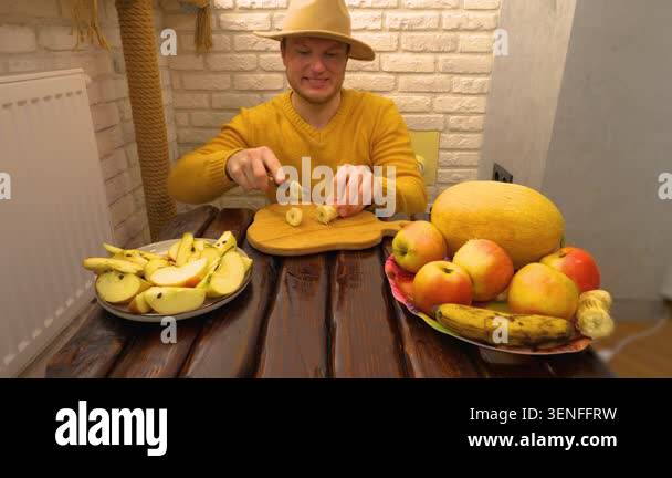 A man prepares a fruit salad. A young man in the kitchen with fruit ...