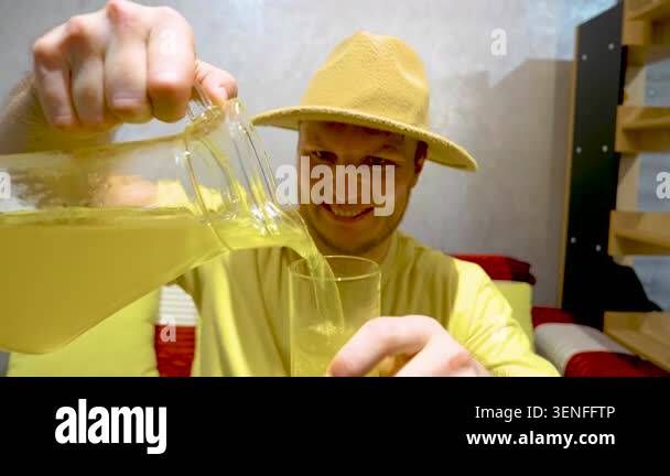 Pour yellow lemonade from a jug into a glass. Man with orange juice ...