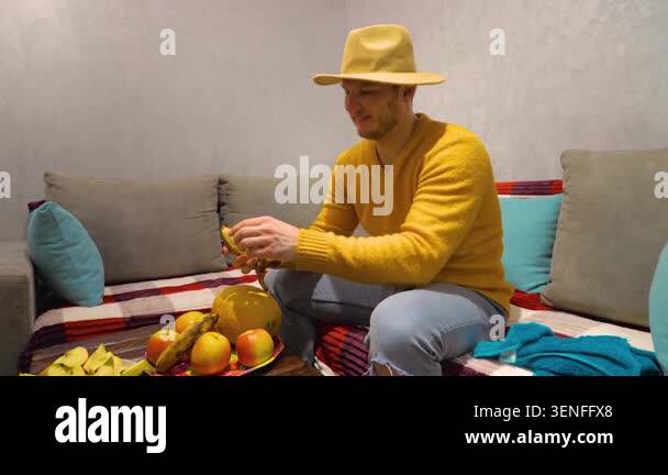 A man eats fruit at home at a table in the living room. Fruits in a ...