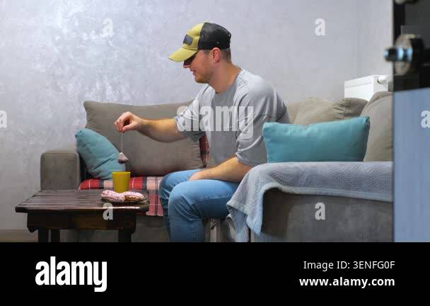 A young and stylish man is having breakfast at home in the living room ...