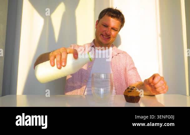 A smiling, young and handsome man pours milk from a plastic bottle into ...