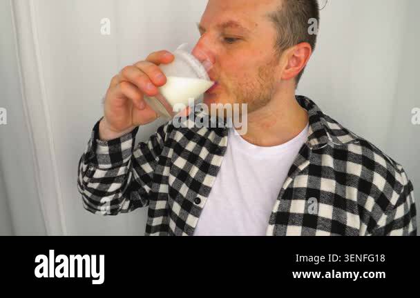 A man drinks milk from a transparent glass, drinking white yogurt, slow ...