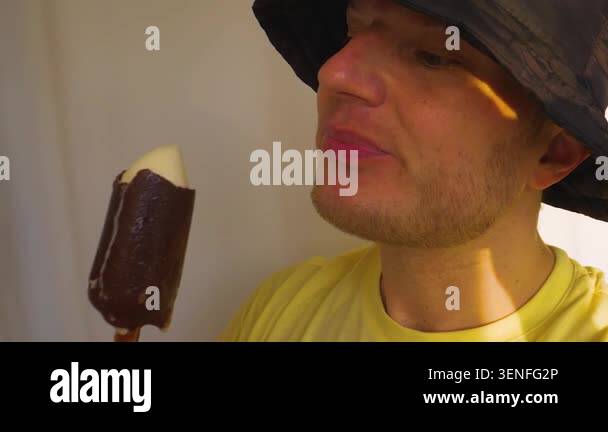 A young guy eats ice cream on a wooden stick, close-up, chocolate ice ...