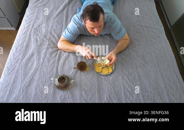 A young man has breakfast with tea while lying on the bed in bed ...