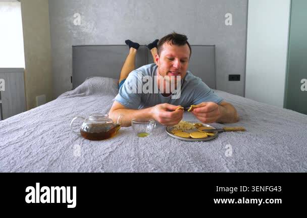 A young man has breakfast with tea while lying on the bed in bed ...