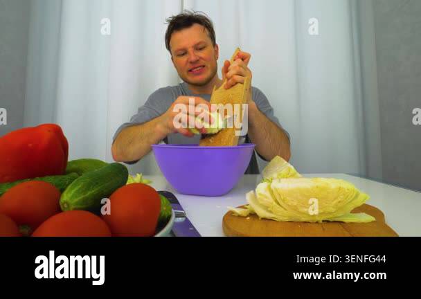 A man is preparing a vegetable salad, cutting white cabbage in the ...