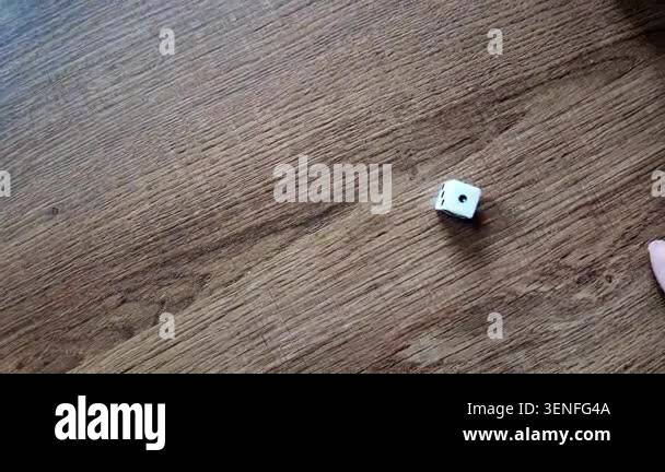 Close up of a man hand throwing a white gaming die on a textured wooden ...