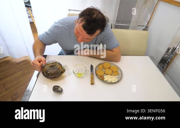 A man pours brewed tea from a teapot into a cup on a white table. Drink ...