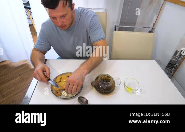A young man has breakfast with tea while sitting in the kitchen. Spread ...